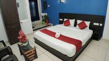 Quarto de hotel com cama, escrivaninha, cadeira, guarda-roupa, espelho, pia e planta em vaso.