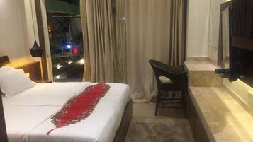 Quarto de hotel com cama, secretária, cadeira e televisão.