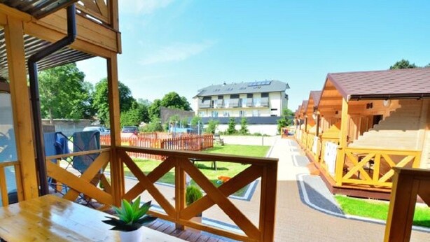 Um deck de madeira com uma mesa e um vaso de planta, com vista para uma fileira de cabanas de madeira e um edifício ao fundo.