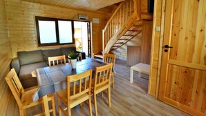 Interior de uma cabana de madeira com uma mesa de jantar, cadeiras, um sofá, uma escada e uma janela grande.