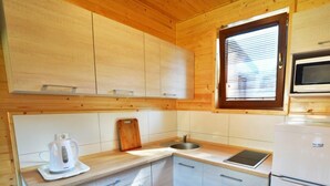Cozinha compacta com armários de madeira, pia, chaleira e micro-ondas.