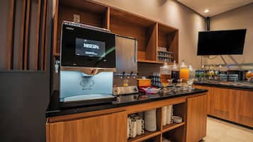 Uma estação de café moderna com máquina Nescafé, televisão de tela plana e diversas bebidas.
