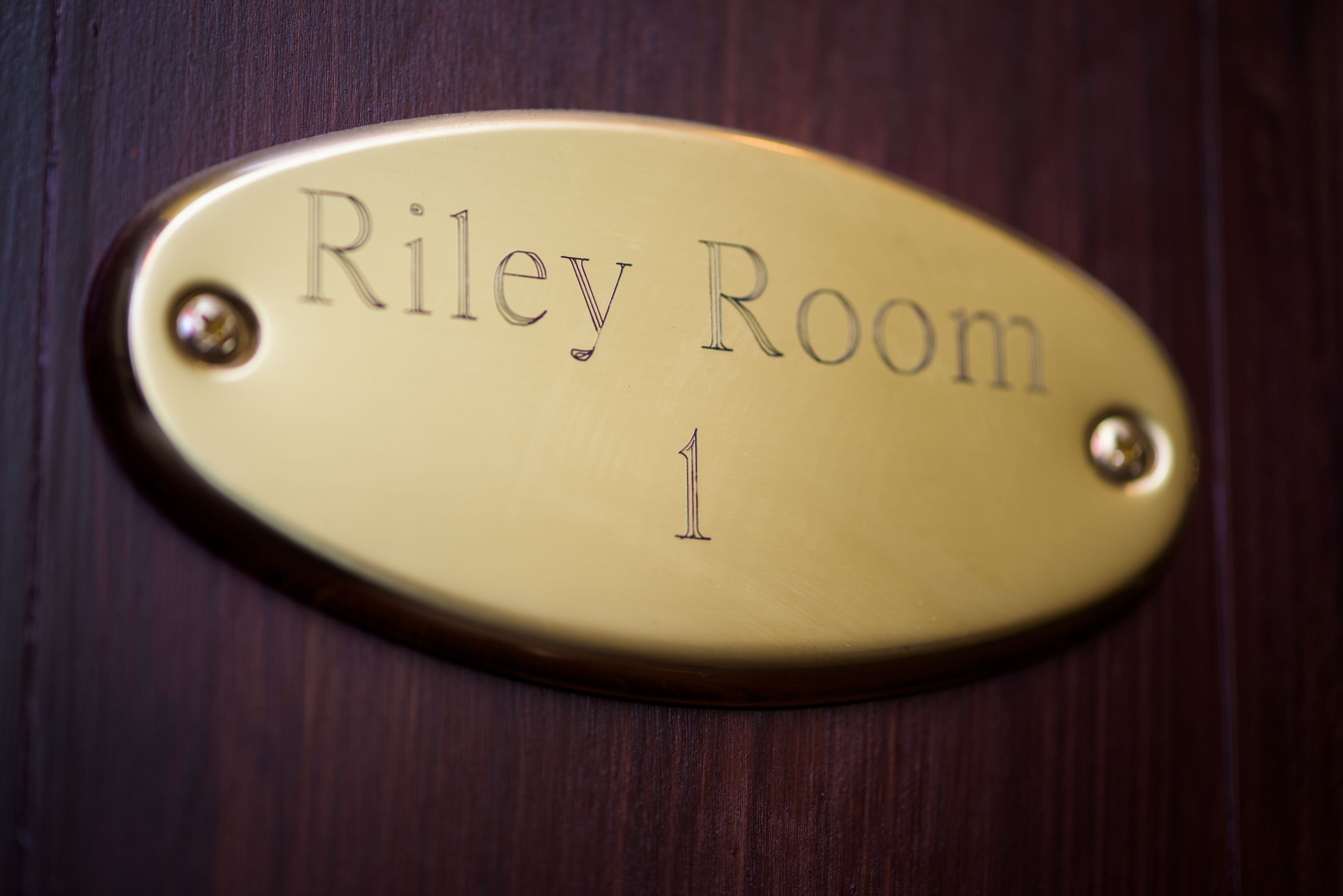 Uma placa de latão com a inscrição 'Riley Room 1' sobre uma superfície de madeira.