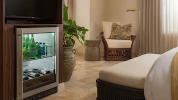 Quarto de hotel com minibar, televisão, planta em vaso, cadeira de vime e abajur.