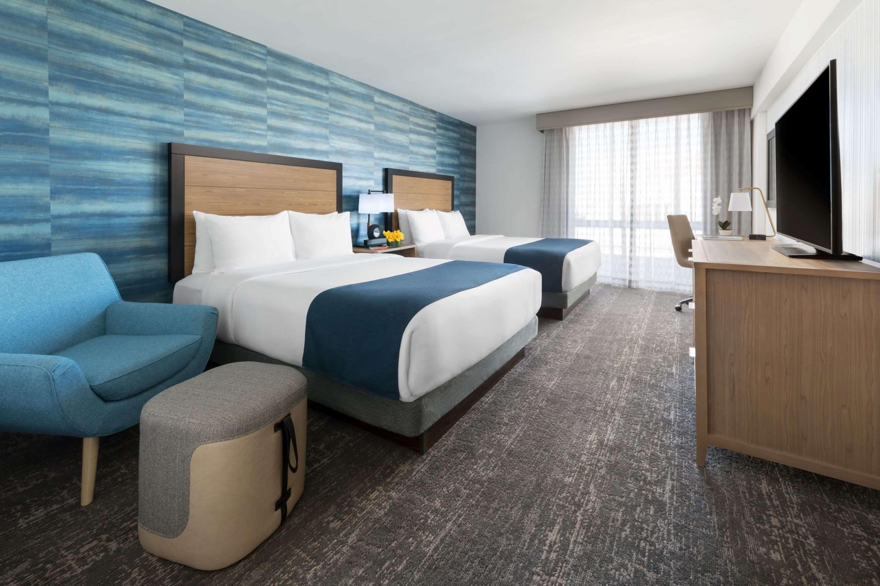 Quarto de hotel com duas camas, uma escrivaninha, uma cadeira e uma televisão.