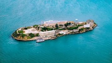 Vista aérea de uma ilha costeira com um grande complexo de edifícios, um farol e um cais com um barco.