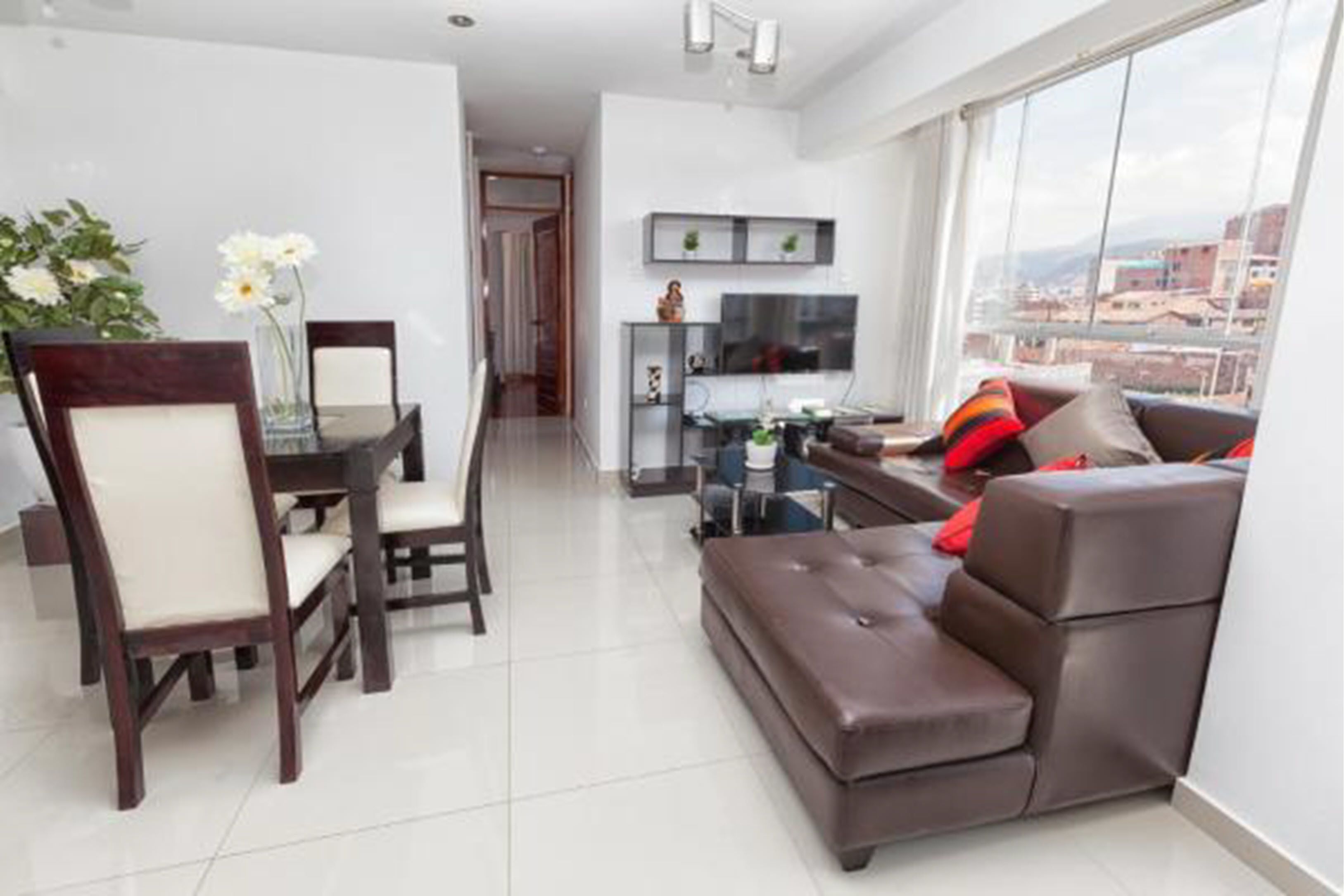 Uma sala de estar moderna com um sofá de couro marrom, uma mesa de jantar com cadeiras e uma janela grande com vista para a cidade.