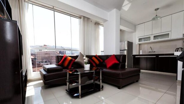 Uma sala de estar moderna com um sofá marrom escuro, uma mesa de centro de vidro e vista da cidade por grandes janelas.