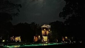 Um edifício com fachada de vidro e área de piscina à noite.