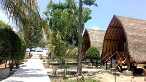 Caminho que leva a construções com telhado de palha, jardim e palmeiras.