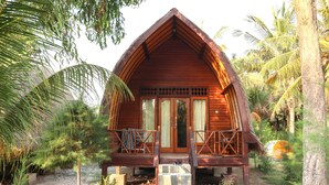 Uma cabana de madeira com varanda, rodeada por vegetação tropical.