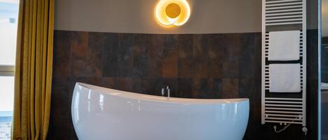 Um banheiro moderno com uma banheira separada, um porta-toalhas fixado na parede e uma luminária circular.