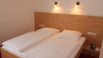 Uma cama de casal com lençóis brancos e duas luminárias fixadas na parede.