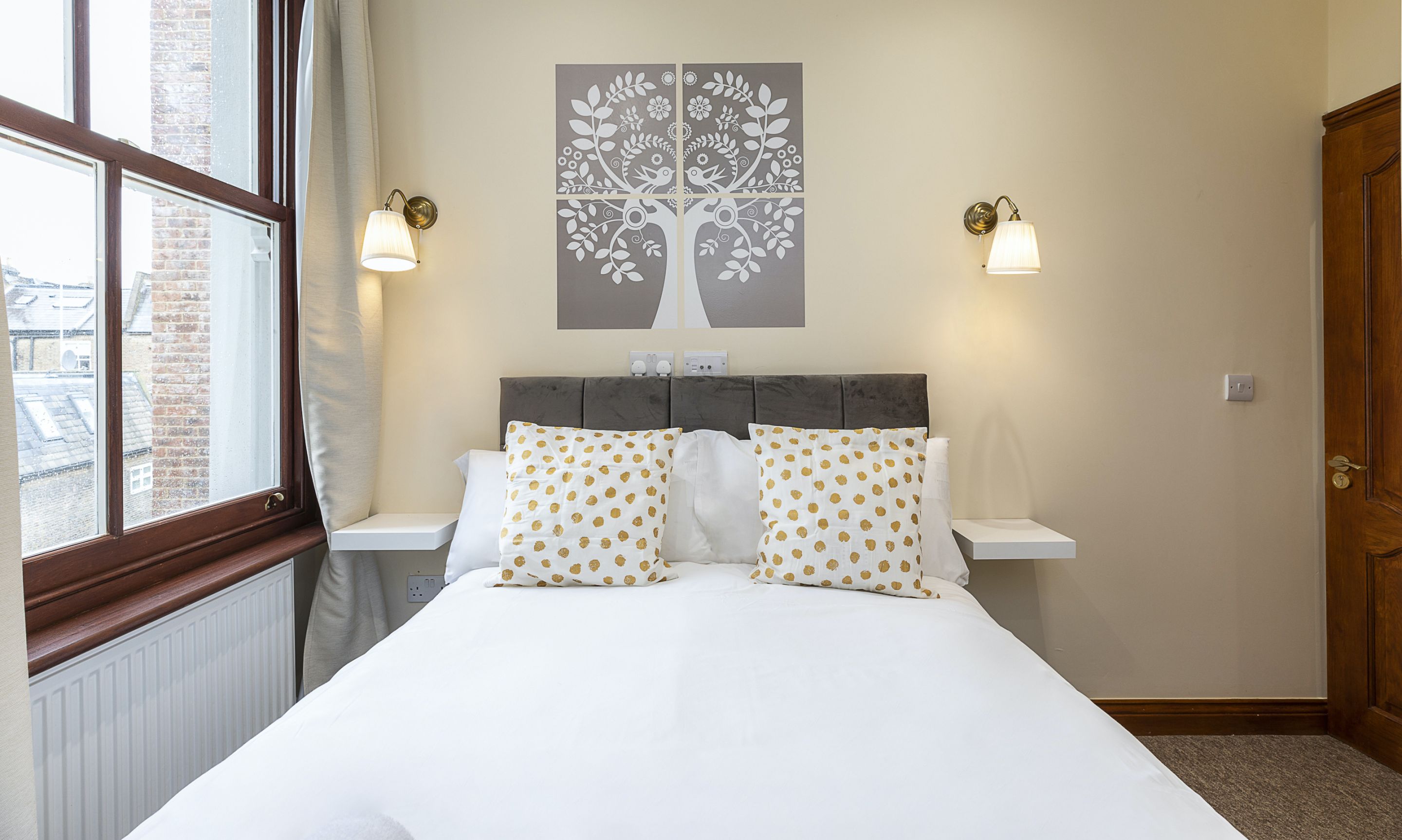 Quarto de hotel com uma cama, duas luminárias de cabeceira, uma janela e uma obra de arte na parede.