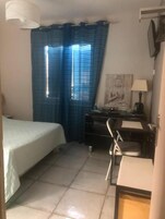 Quarto com cama, escrivaninha, cadeira e cortinas.