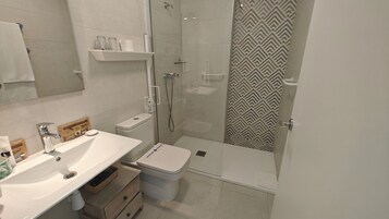 Um banheiro moderno com pia, vaso sanitário e chuveiro brancos. Há prateleiras acima da pia e um cortina de chuveiro estampada.
