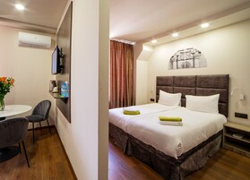 Quarto de hotel com cama, mesa de cabeceira e televisão fixada na parede.