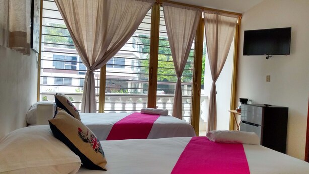 Quarto de hotel com duas camas, televisão e varanda com cortinas.