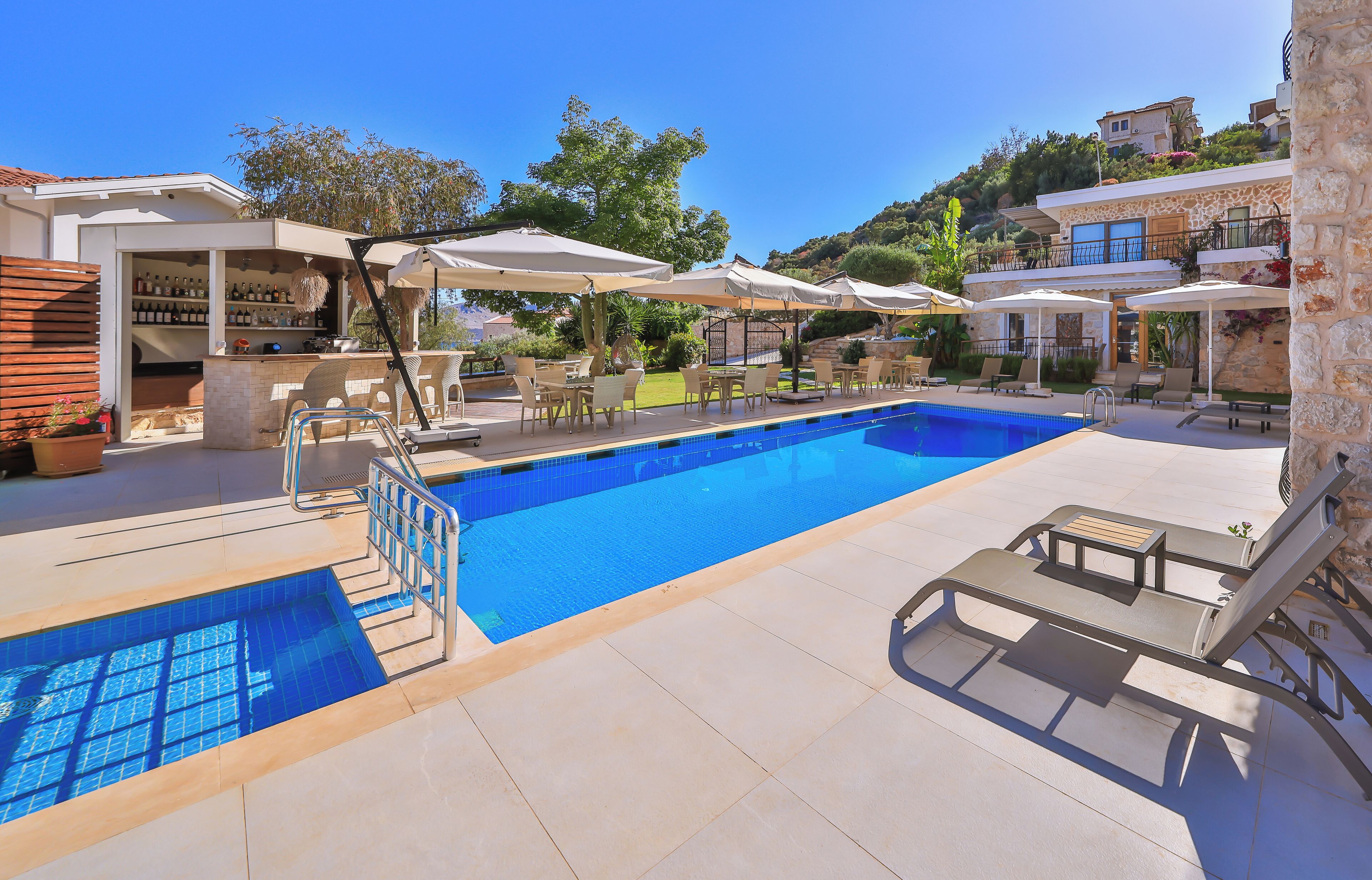 Piscina com espreguiçadeiras e guarda-sóis, rodeada por um pátio com bar e mesas ao ar livre.