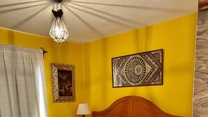 Quarto com cama de madeira, mesa de cabeceira com abajur, quadro na parede e um objeto decorativo.