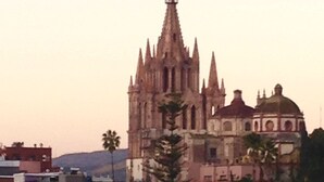 Uma catedral com uma torre alta e uma cúpula, rodeada por edifícios residenciais e palmeiras.