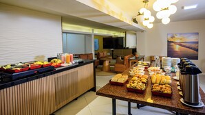 Disposição de buffet com diversos alimentos e uma estação de café em quarto de hotel moderno.