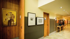 Um corredor com obras de arte emolduradas nas paredes, um banco de madeira e uma porta.