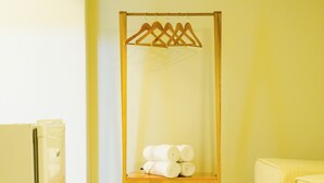 Quarto compacto com um guarda-roupa de madeira, uma cama com colcha amarela e um frigorífico branco.