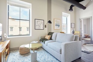 Uma sala de estar moderna com um sofá cinza, uma mesa de centro redonda e uma janela grande.