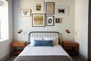 Quarto bem organizado com uma cama, duas mesas de cabeceira e uma parede decorada com quadros.