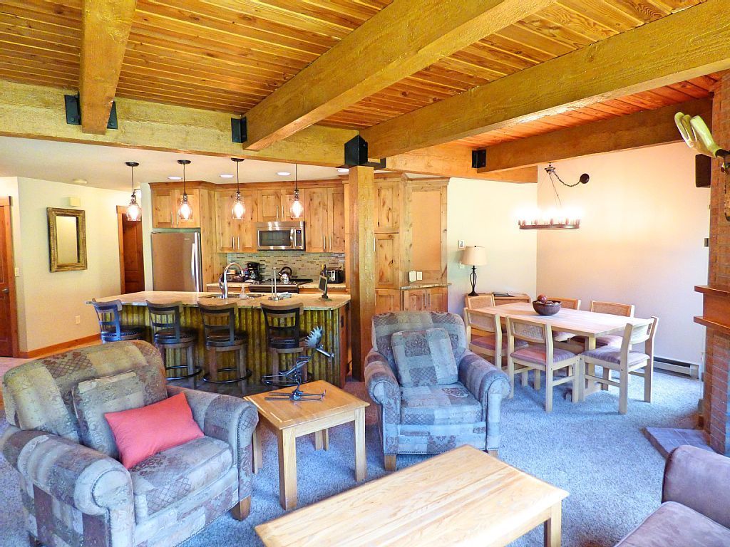 Uma sala de estar acolhedora, com teto de madeira, cozinha com armários de madeira e mesa de jantar com cadeiras.