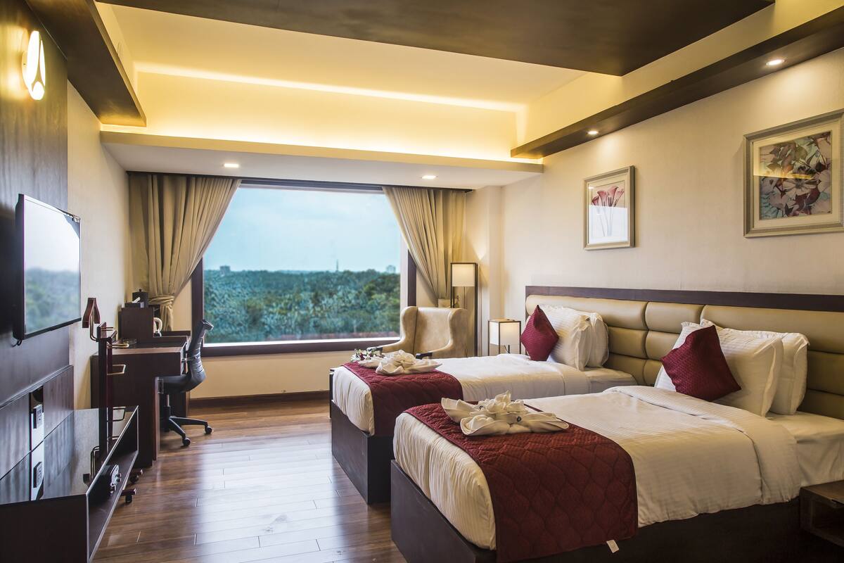 Quarto de hotel com duas camas, uma escrivaninha, uma cadeira e uma televisão.