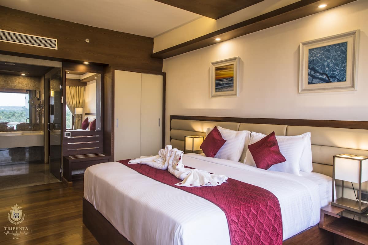 Quarto de hotel com uma cama grande, mesa de cabeceira, luminária e um quadro na parede.