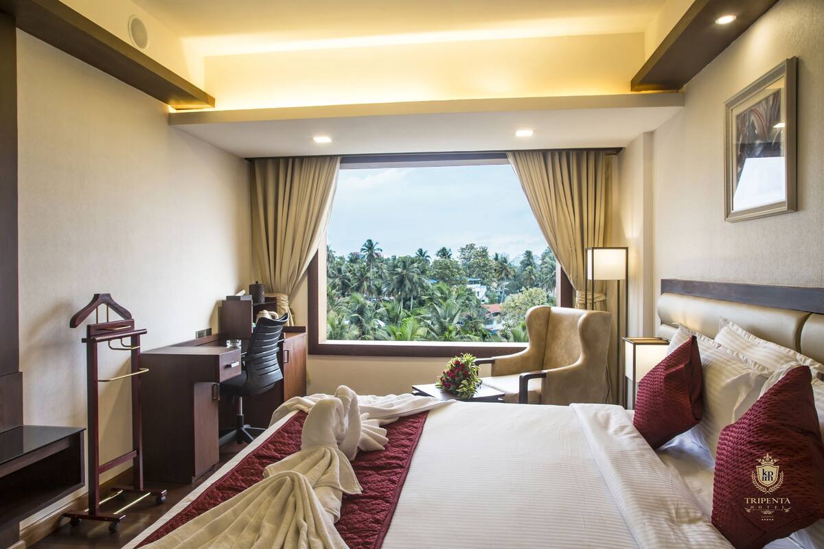 Quarto de hotel com cama grande, uma escrivaninha, uma cadeira e vista para o exterior.