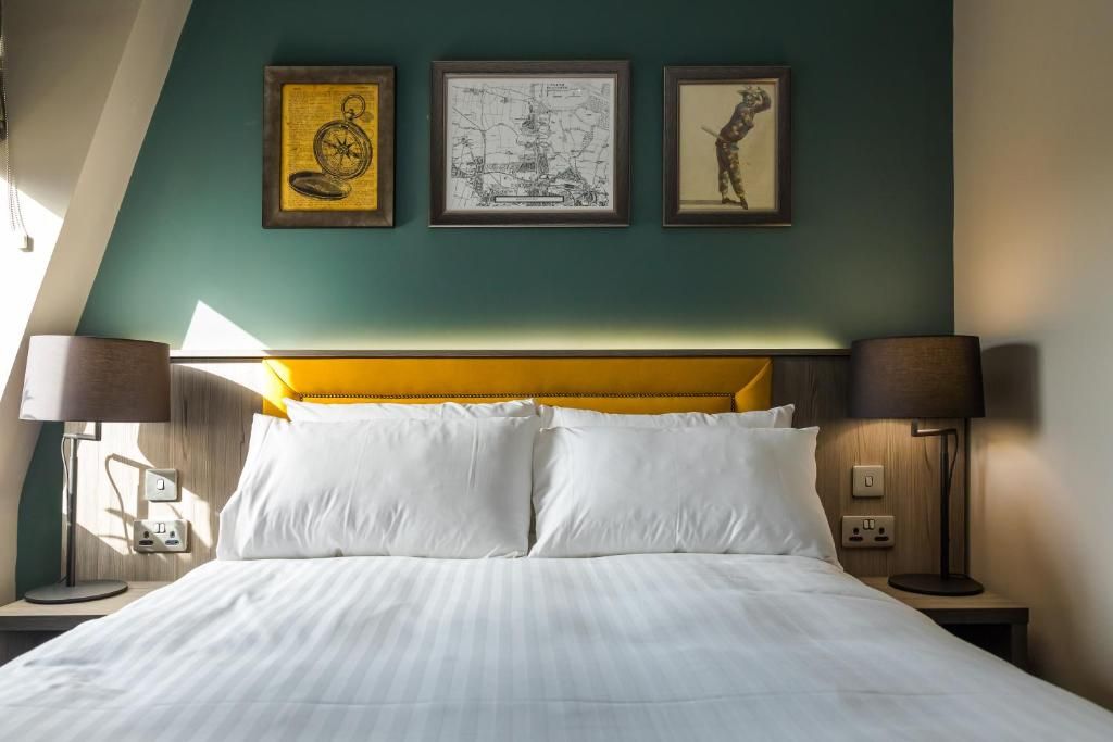 Quarto de hotel com cama, duas luminárias laterais, mapa fixado na parede e quadro emoldurado.