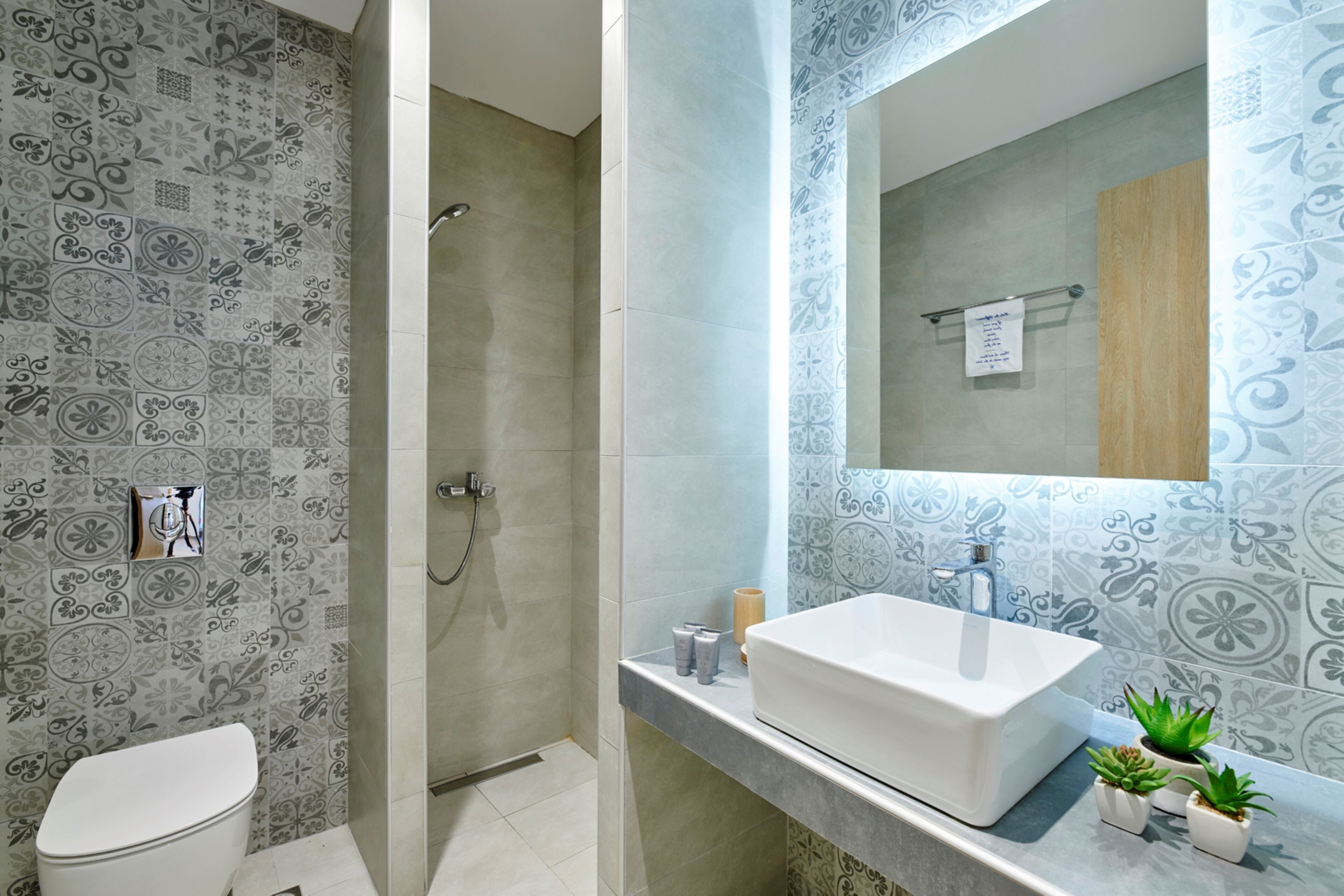 Um banheiro com azulejos estampados, pia branca e espelho.