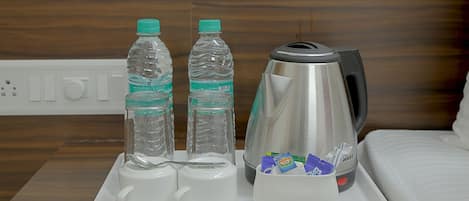 Uma bandeja com duas garrafas de água, uma cafeteira e outra bandeja com sachês sobre uma mesa de madeira em um quarto de hotel.