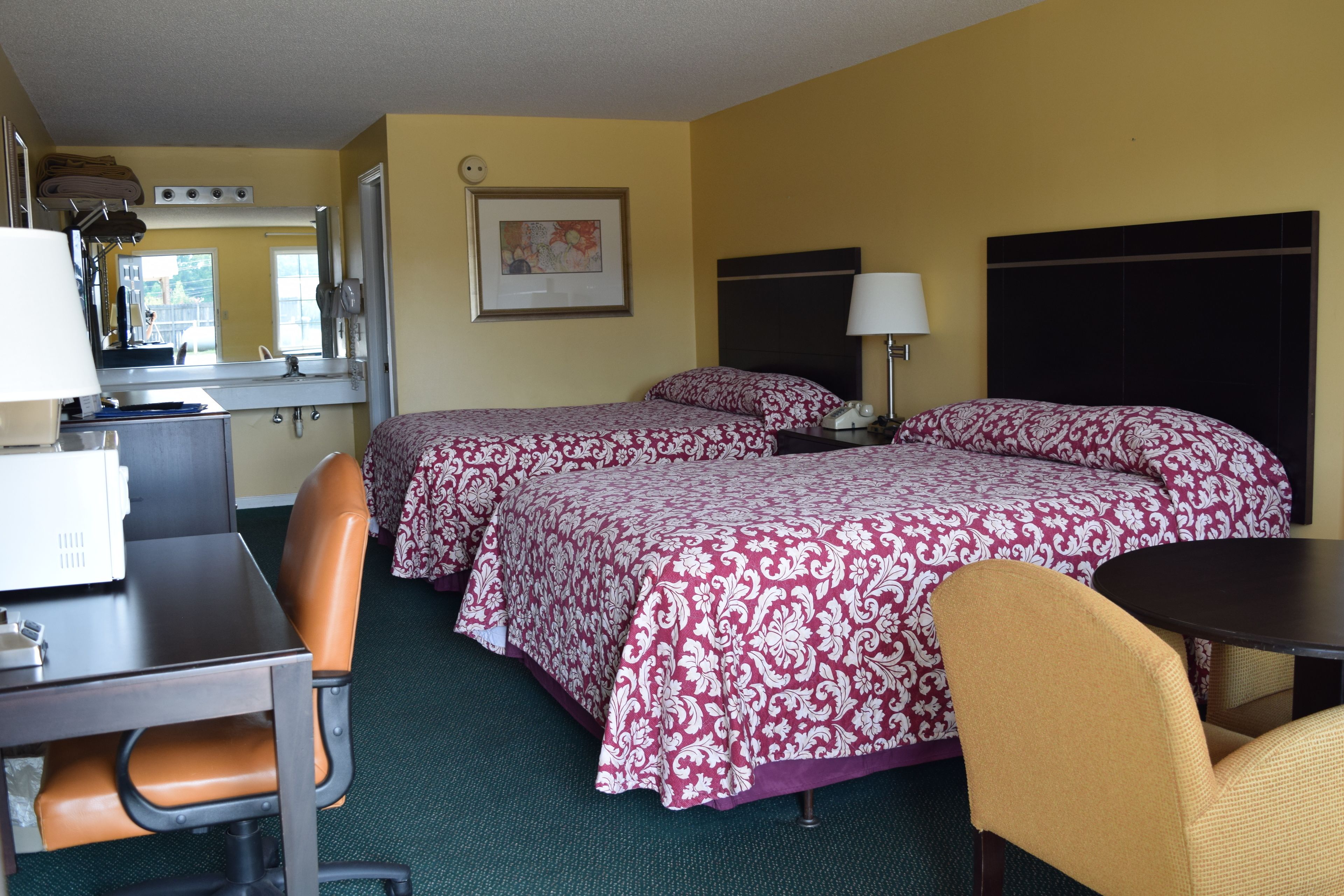 Quarto de hotel com duas camas, uma escrivaninha, uma cadeira, uma mesa e um espelho.