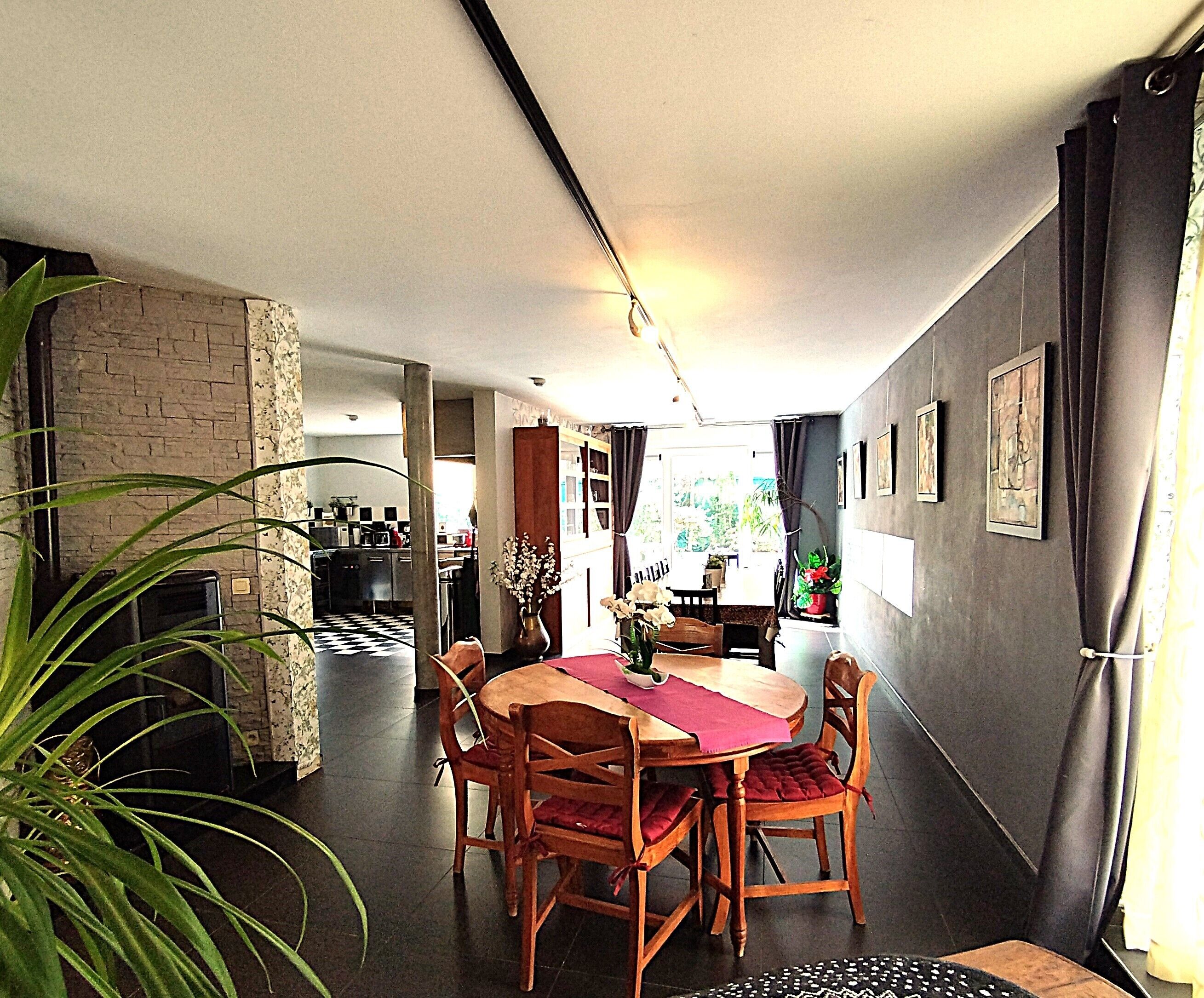 Uma área de refeições com mesa e cadeiras, um vaso com flores e uma parede de tijolos.