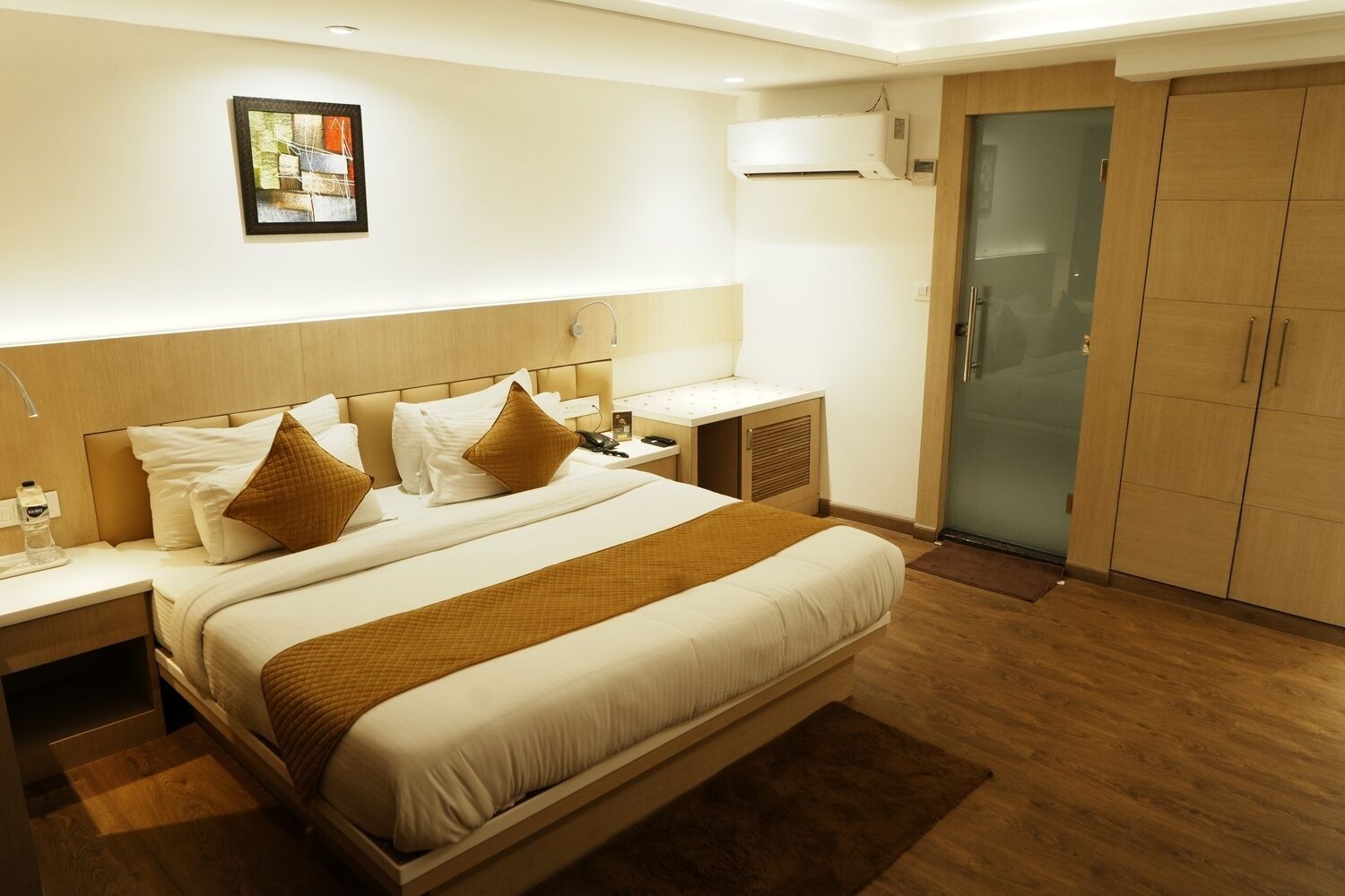 Quarto de hotel com uma cama grande, mesas de cabeceira, guarda-roupa e ar condicionado fixado na parede.