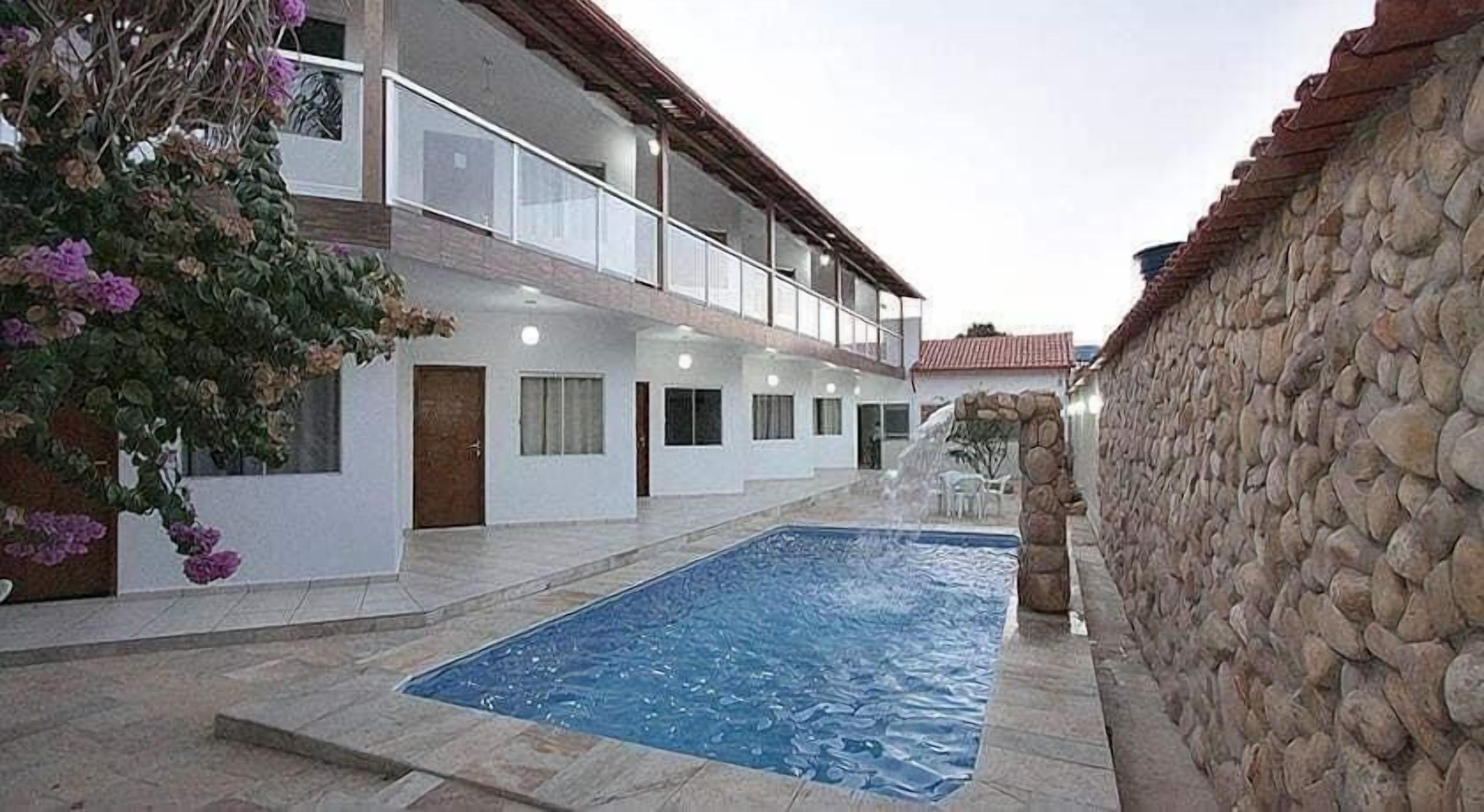Uma área de piscina com muro de pedra, um edifício branco com varandas e uma porta.