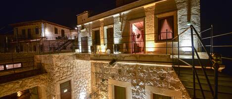 Edifício de pedra com vários níveis, escadas e varandas, com entrada bem iluminada e diversas janelas.