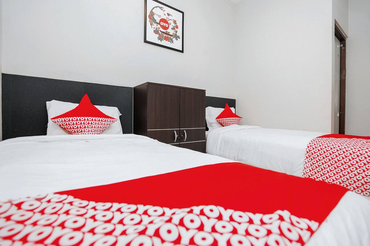 Quarto de hotel com duas camas, um guarda-roupa de madeira escura e um quadro na parede.
