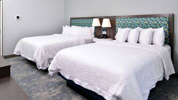 Quarto de hotel com duas camas, cabeceira com padrão decorativo, mesa de cabeceira com luminárias e tapete estampado.