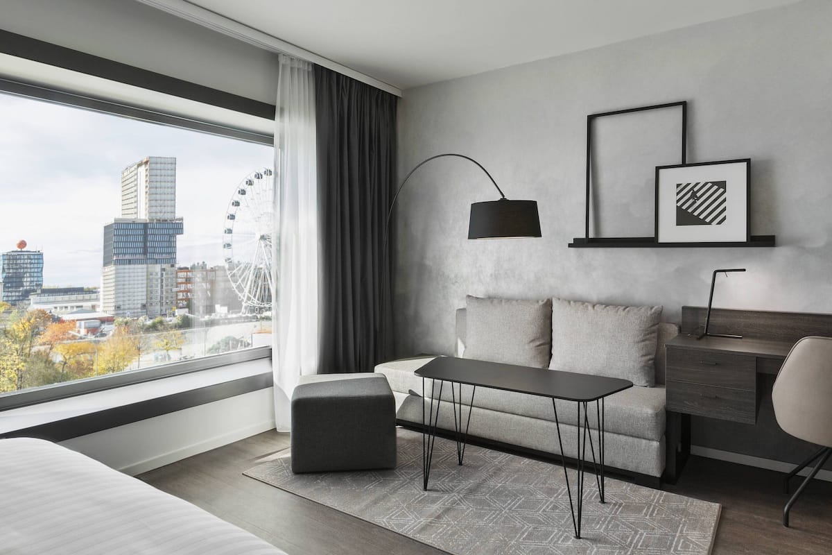 Quarto de hotel moderno com uma janela grande, um sofá, uma mesa e uma cadeira.