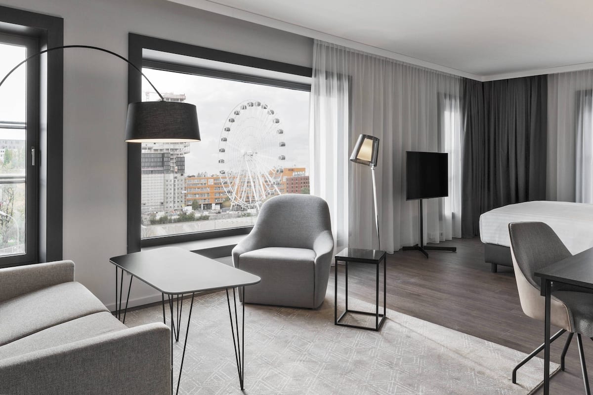Quarto de hotel moderno com uma grande janela, uma cadeira, uma cama, uma escrivaninha e um abajur.