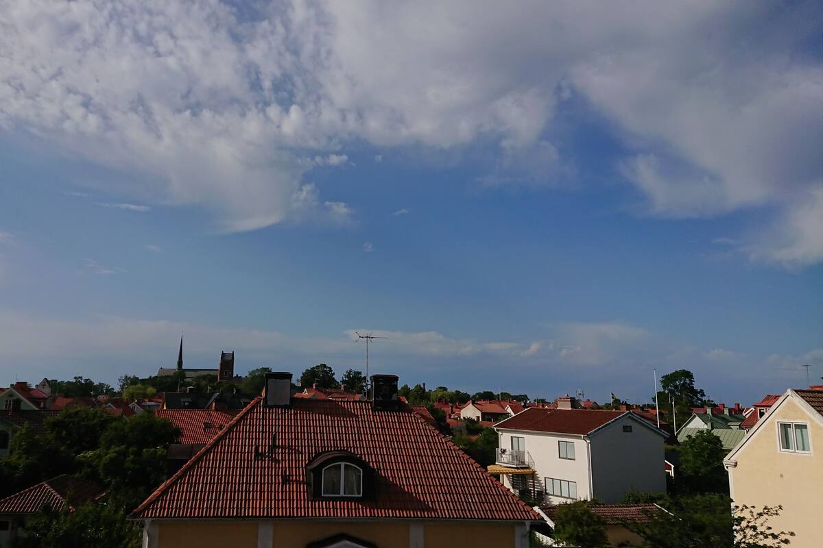 Um bairro residencial com telhados de telha vermelha, uma torre de igreja e céu claro.