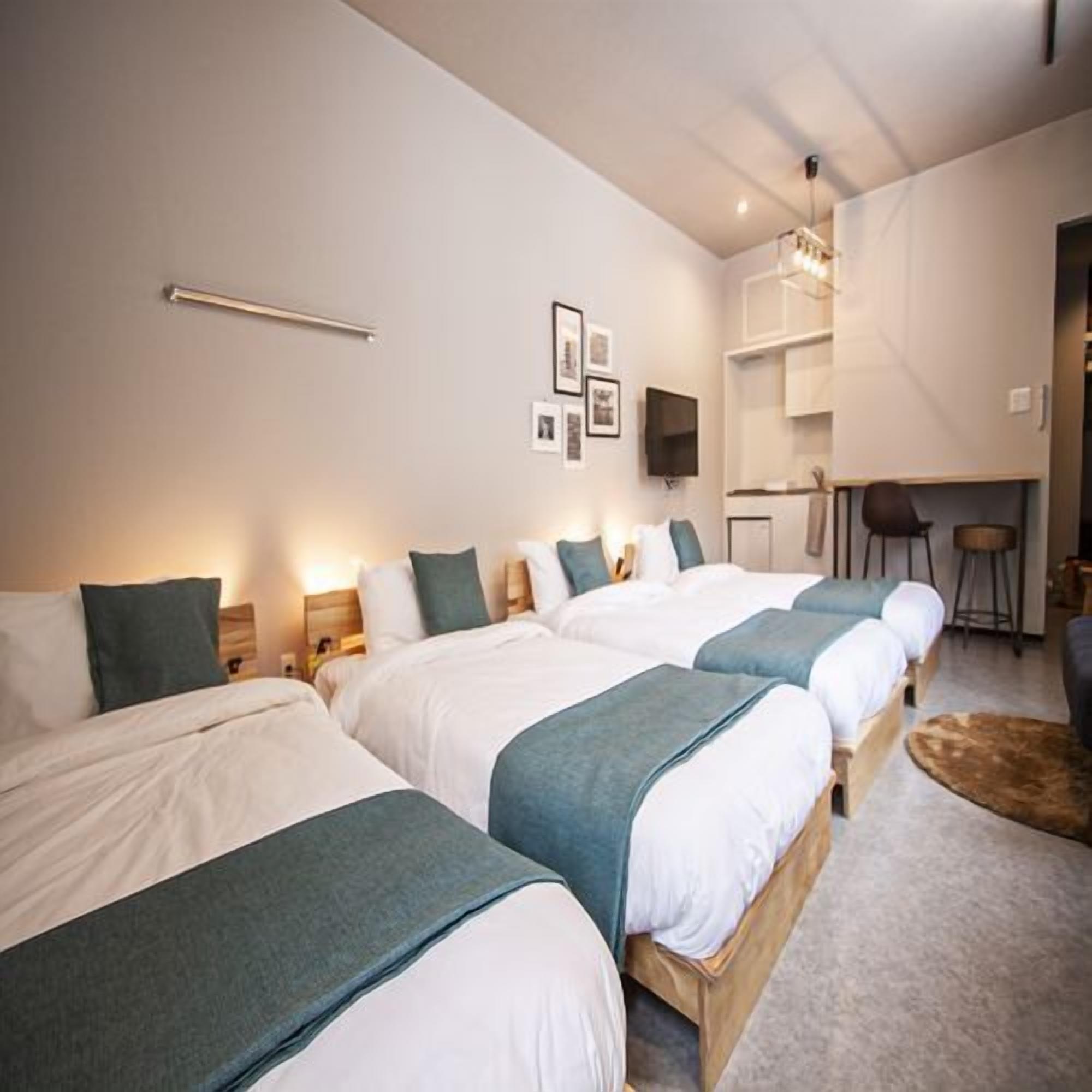 Quarto de hotel com três camas, uma escrivaninha e uma televisão.