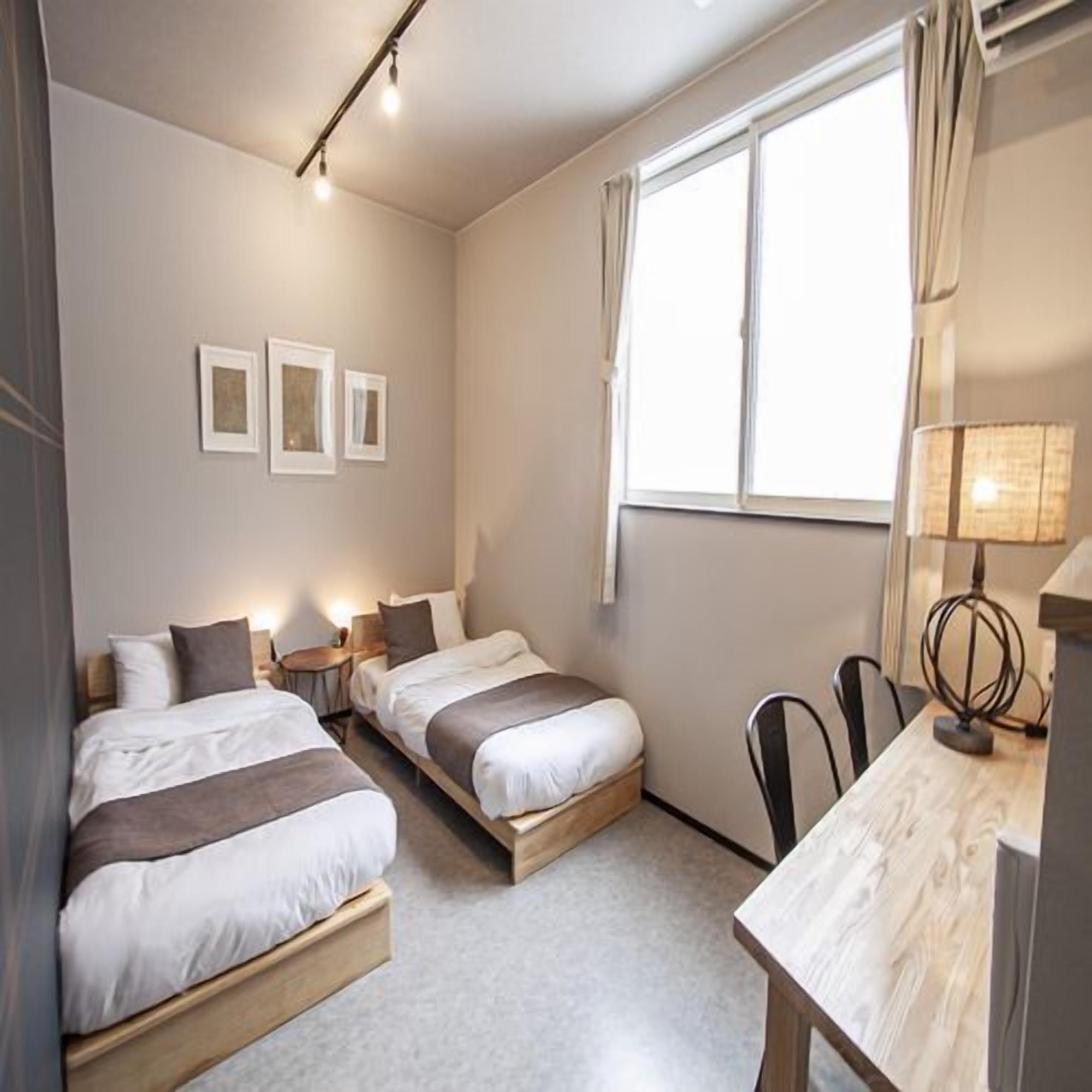 Quarto com duas camas, uma escrivaninha e uma janela.
