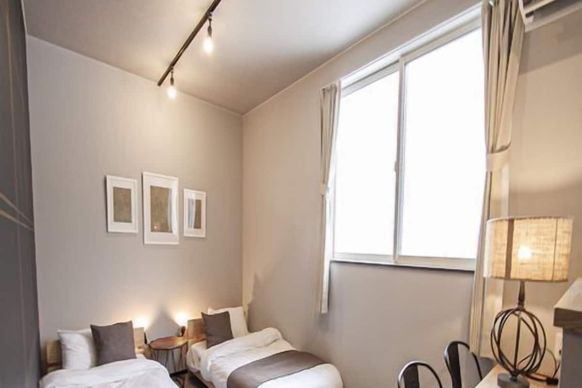 Quarto com duas camas, uma escrivaninha e uma janela.